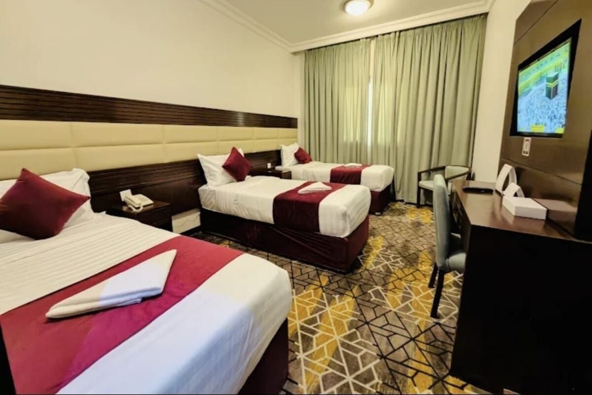 Quarto de hotel com duas camas, uma escrivaninha, televisão e carpete estampado.