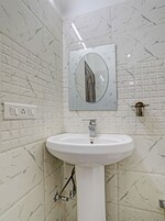 Uma casa de banho com uma pia branca, um espelho com moldura decorativa e uma luminária fixada na parede.