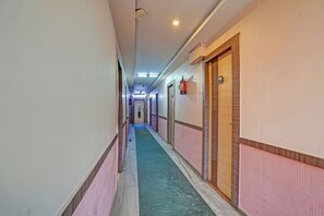 Corredor de hotel com portas em ambos os lados, um extintor de incêndio fixado na parede e uma luminária no teto.