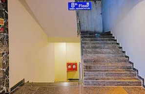 Escadaria que leva ao oitavo andar, com detector de incêndio e caixa de emergência vermelha na parede.