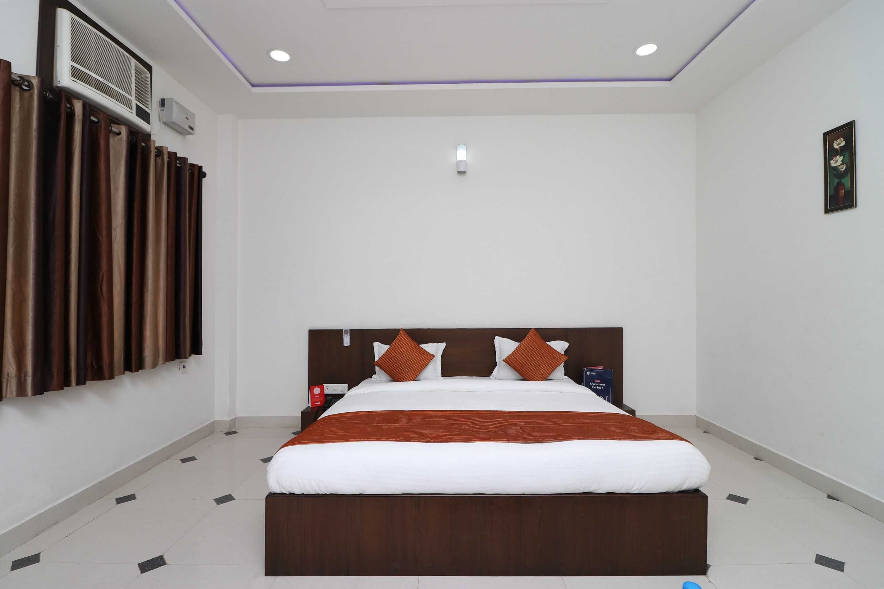 Quarto de hotel com uma cama grande, mesa de cabeceira, ar condicionado fixado na parede e luminária no teto.