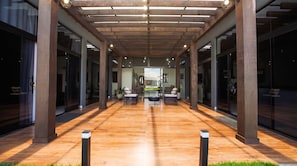 Interior moderno com piso de madeira, divisórias de vidro e área de estar central com mesa redonda e cadeiras.