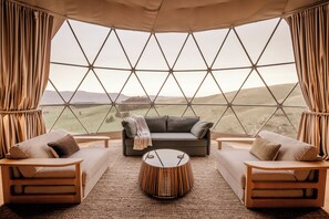 Uma área de estar acolhedora com vista para uma paisagem montanhosa através de uma estrutura de janela geométrica.