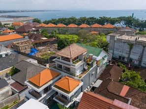 Uma área residencial costeira com edifícios modernos e tradicionais, vista clara para o mar e um farol imponente ao longe.
