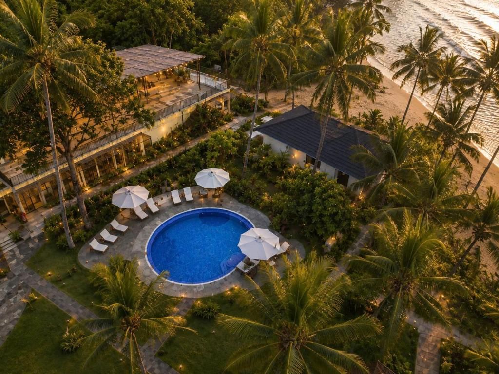 Vista aérea de um resort com piscina, cercada por palmeiras e espreguiçadeiras.