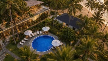 Vista aérea de um resort com piscina, cercada por palmeiras e espreguiçadeiras.