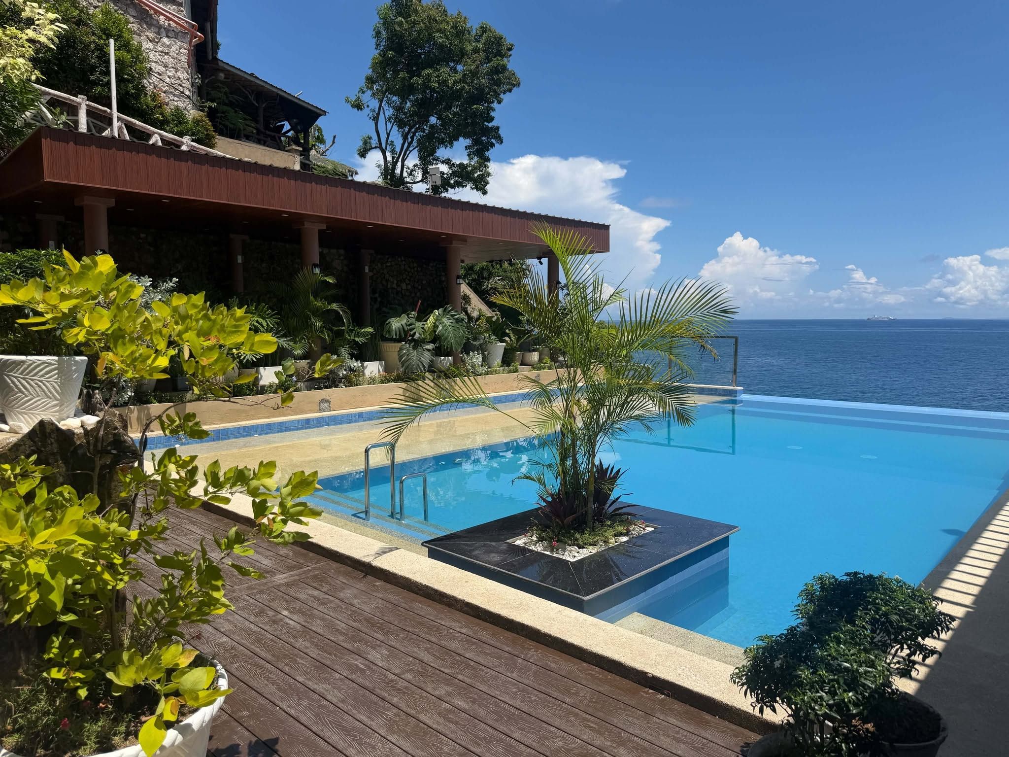Uma área de piscina com vista para o oceano, cercada por plantas em vasos e um deck de madeira.