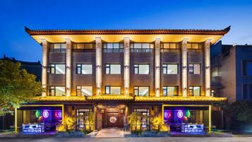Um edifício de vários andares com estilo arquitetônico tradicional, apresentando uma entrada central com porta decorativa e duas entradas laterais com sinalização iluminada.