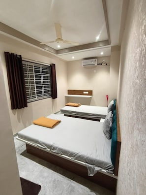 Quarto de hotel com cama, ar condicionado, janela com cortinas e ventilador de teto.