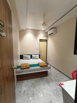 Quarto de hotel com cama, porta de madeira, ventilador de teto, ar condicionado e uma cadeira vermelha.