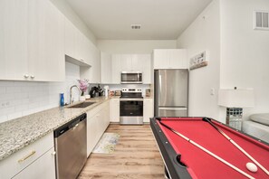 Cozinha moderna com armários brancos, eletrodomésticos de aço inoxidável e mesa de bilhar.