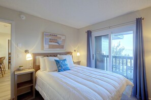 Quarto de hotel com uma cama, mesa de cabeceira, luminária, um quadro na parede e vista exterior pela janela.