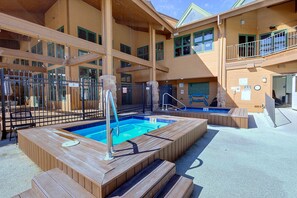 Área de piscina com hidromassagem, deck de madeira e um cercado.