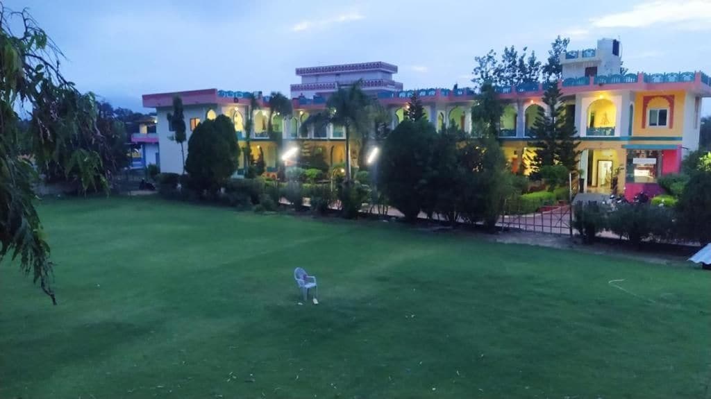 Hotel com gramado bem cuidado, céu claro e edifício tradicional com vários andares e varandas.
