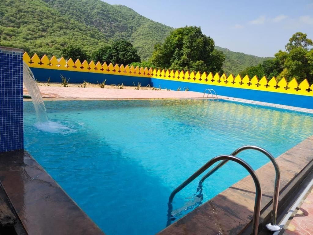 Piscina com borda em azulejos azuis e amarelos, escada de metal e cascata.