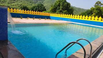 Piscina com borda em azulejos azuis e amarelos, escada de metal e cascata.