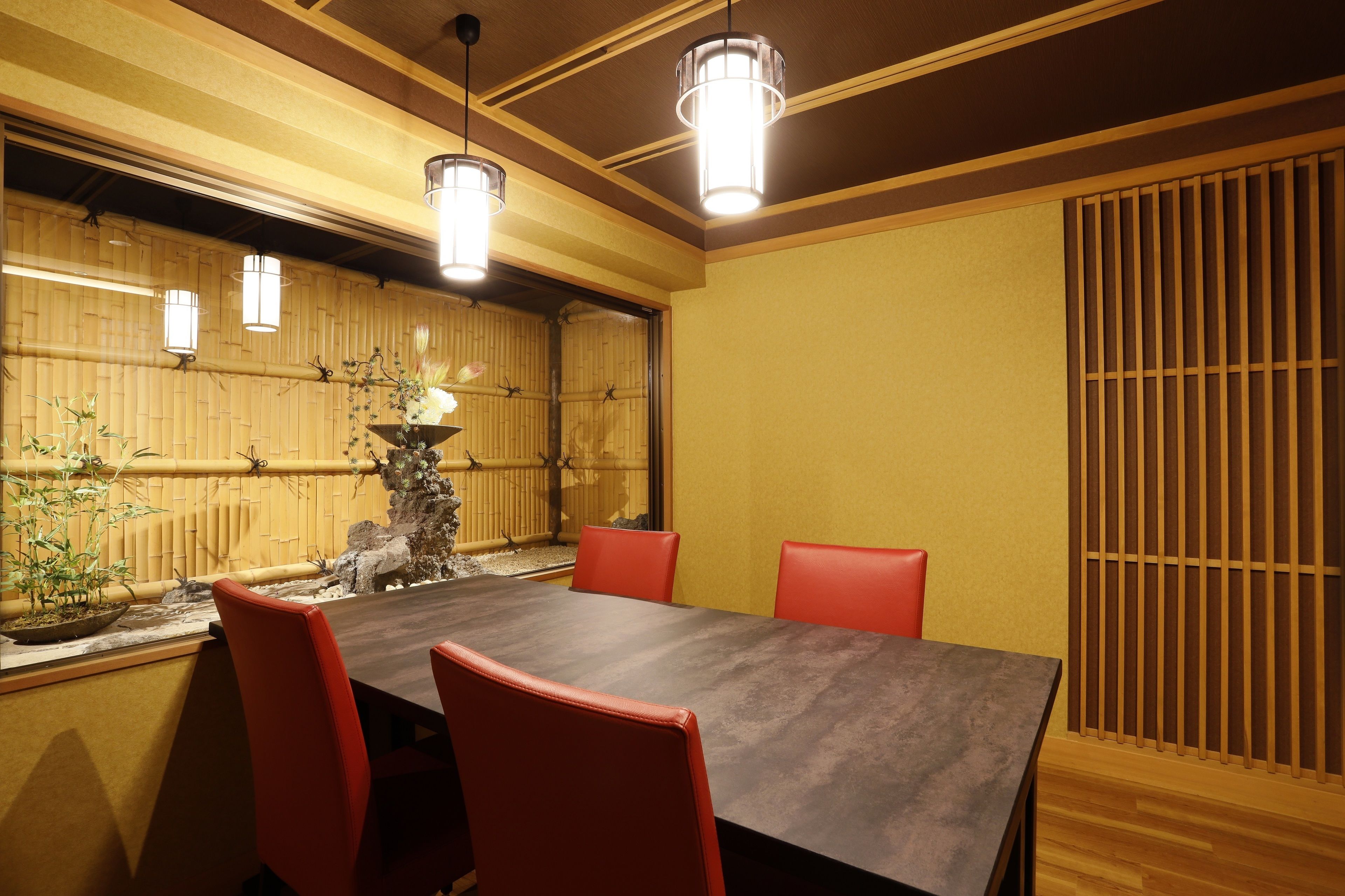 Uma sala de conferências com uma mesa comprida, cadeiras vermelhas e luminárias pendentes.