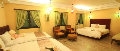 Quarto de hotel com duas camas, área de estar com cadeiras, uma pequena mesa e cabeceira decorativa.