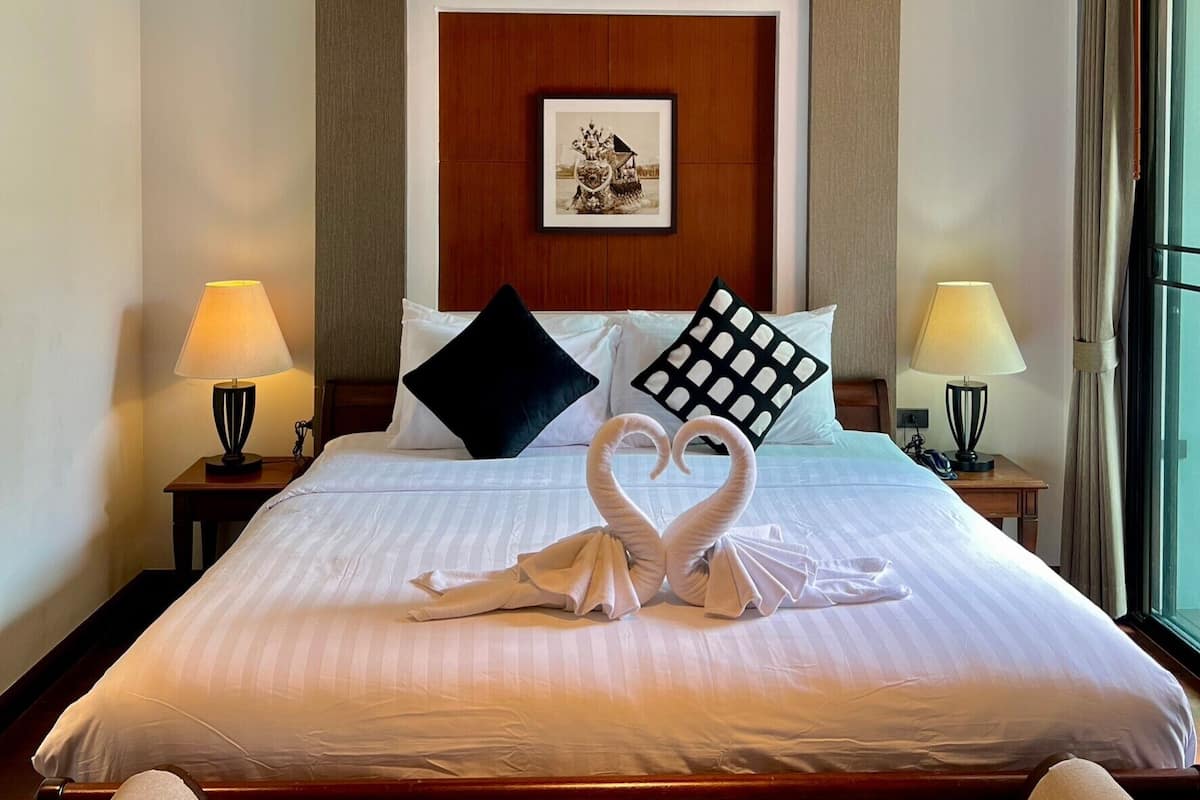 Quarto de hotel com uma cama grande, duas luminárias de cabeceira, um quadro na cabeceira e uma janela com cortinas.