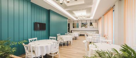 Uma sala de jantar com mesas e cadeiras brancas, paredes verde-água e um candelabro.