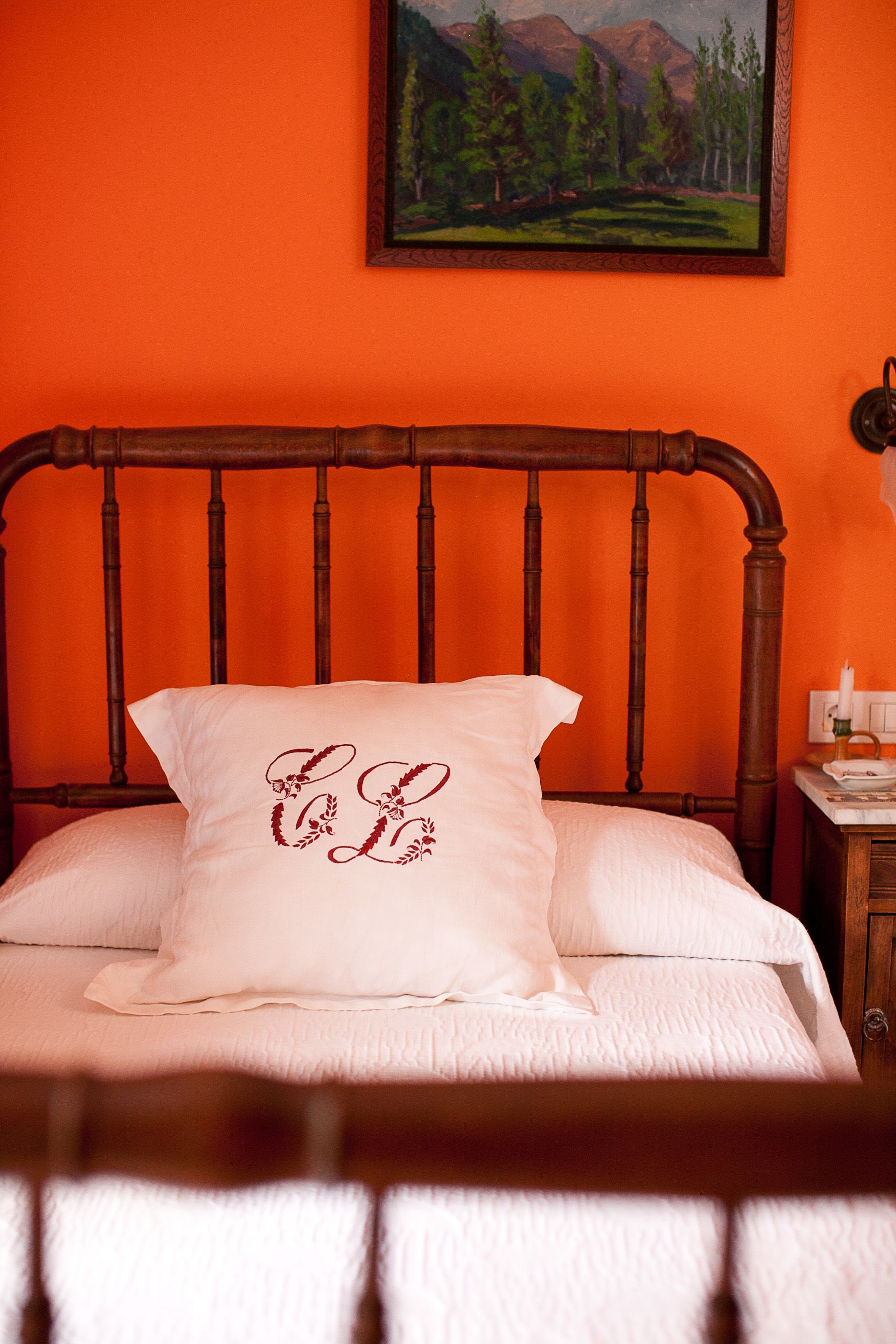 Cama com cabeceira de madeira, roupa de cama branca e travesseiro com iniciais bordadas.
