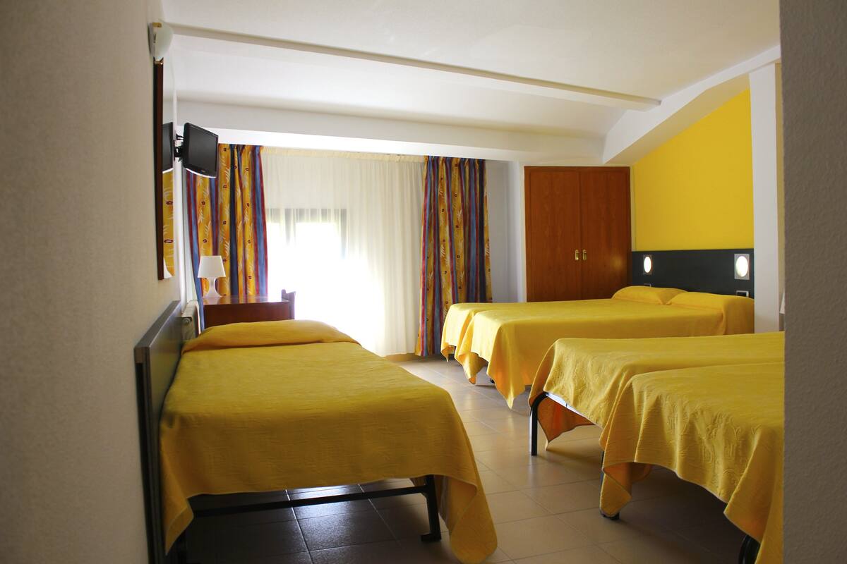 Quarto de hotel com duas camas de solteiro, televisão e janela com cortinas.