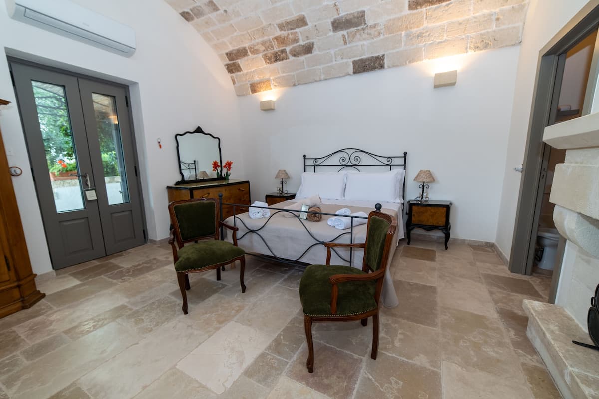 Quarto com cama, duas cadeiras, cômoda e espelho.