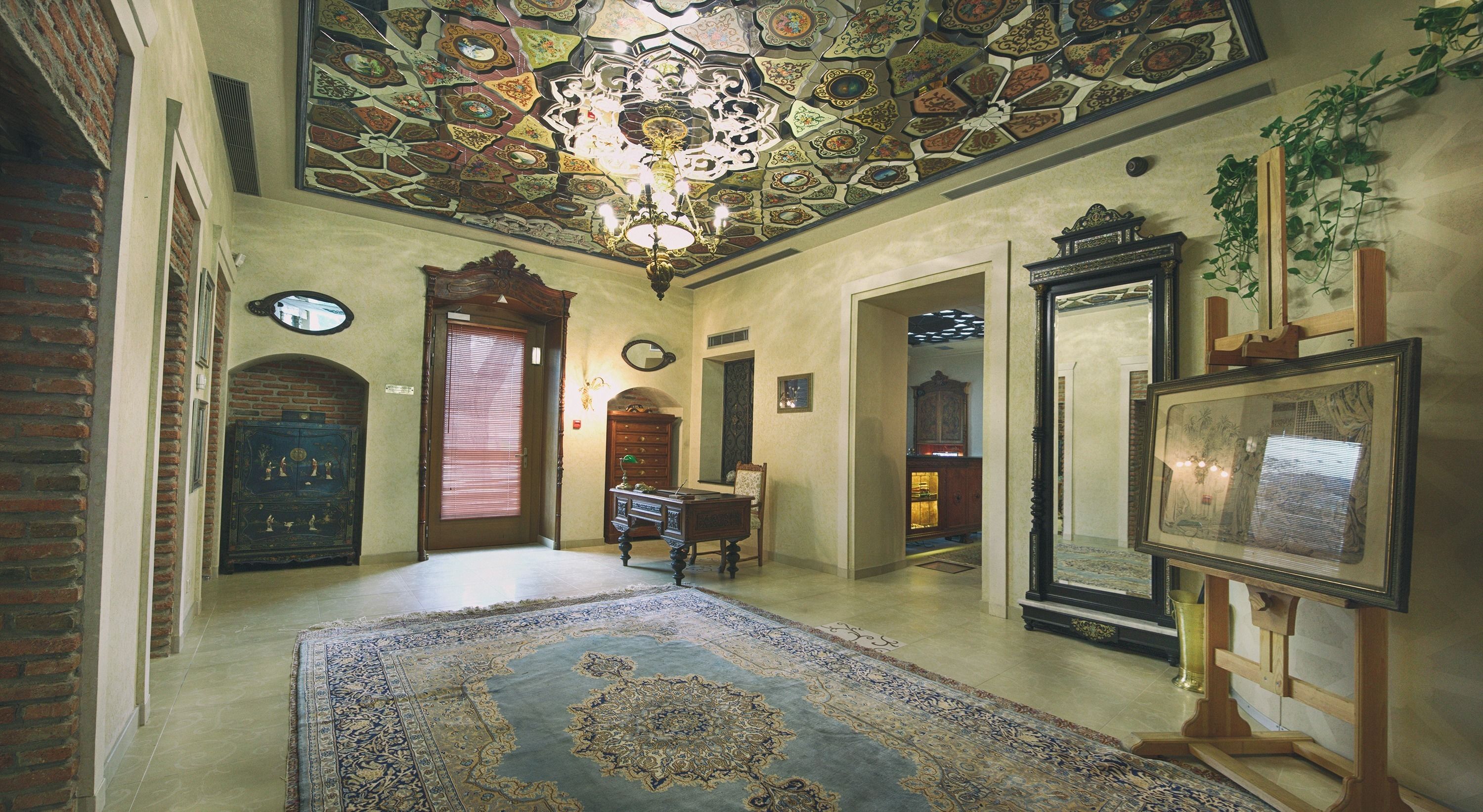 Quarto espaçoso com um teto grande e ricamente decorado, uma escrivaninha de madeira, uma cadeira e um quadro na parede.