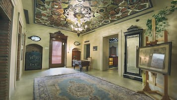 Quarto espaçoso com um teto grande e ricamente decorado, uma escrivaninha de madeira, uma cadeira e um quadro na parede.