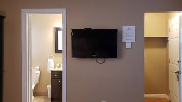 Quarto com televisão fixada na parede, porta para o banheiro e um aviso na parede.