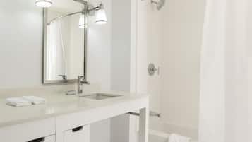 Um banheiro moderno com toucador branco, um espelho grande, duas pias, chuveiro com porta de vidro e porta-toalhas.