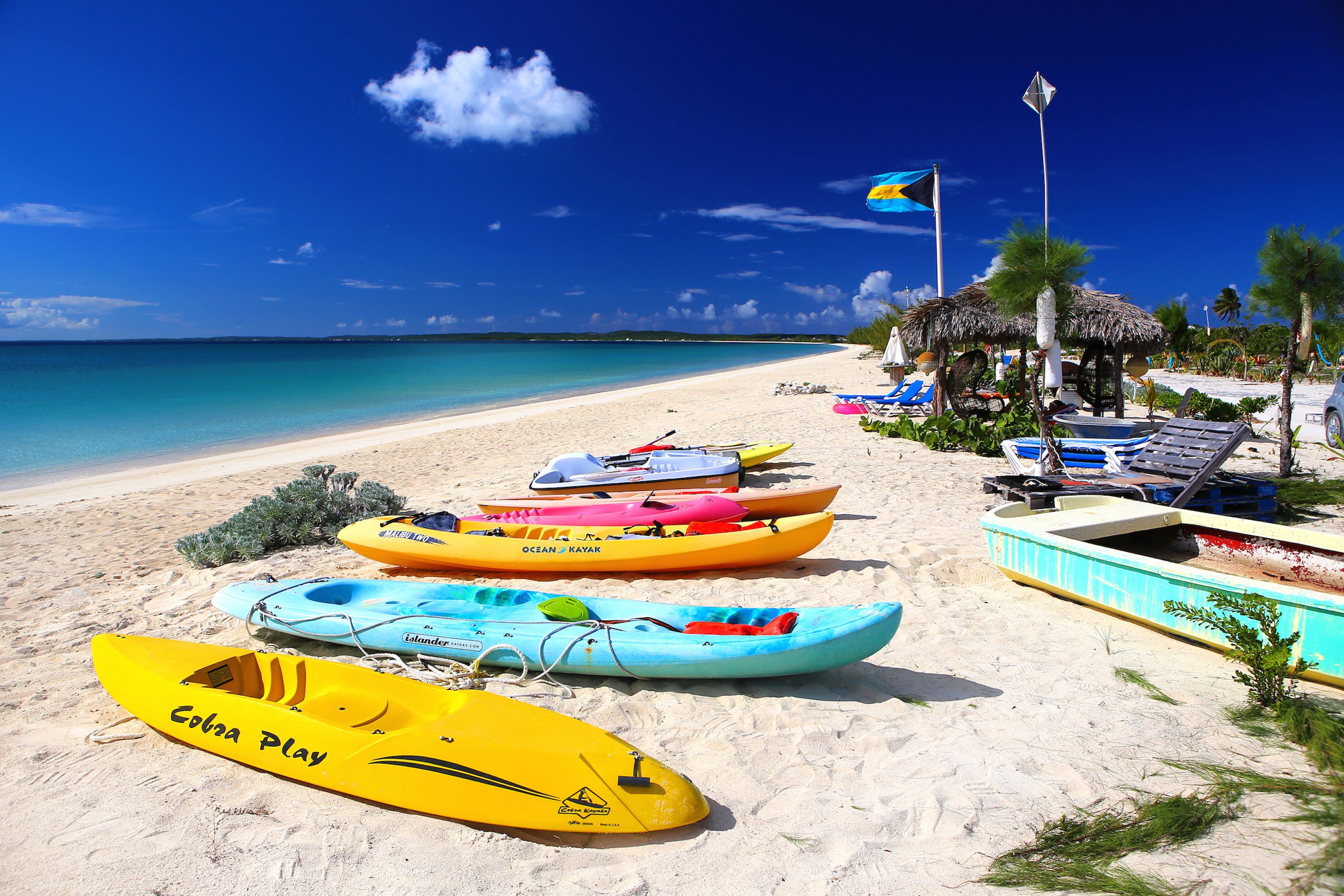 Uma praia com caiaques, cadeiras de praia e piscina.