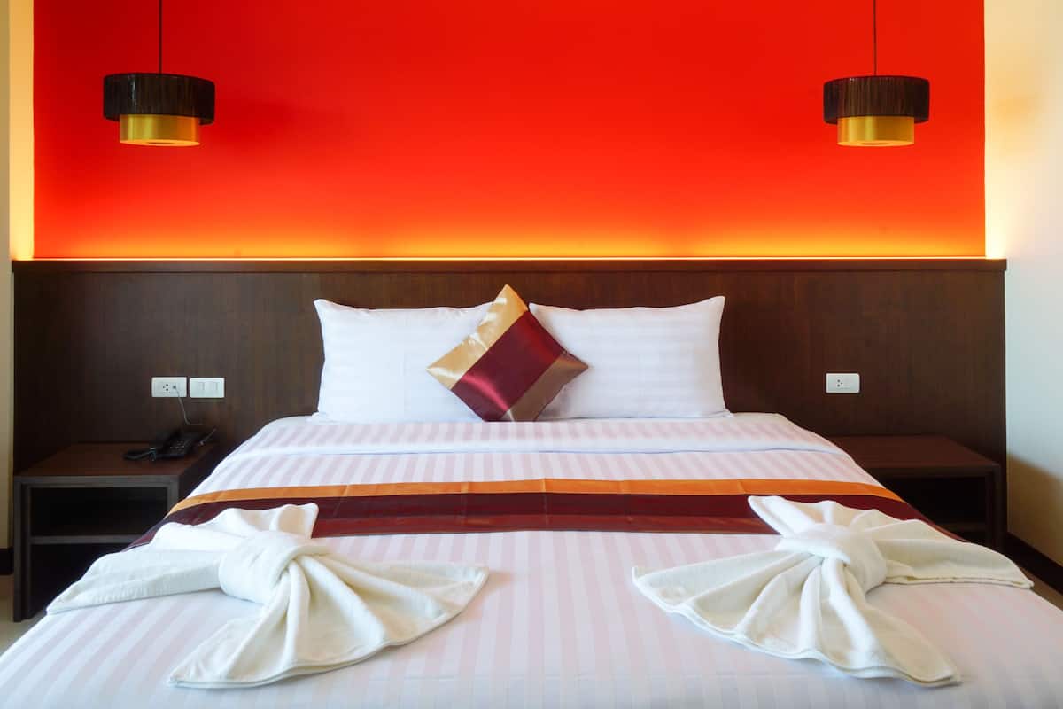 Quarto de hotel com uma cama grande, duas mesas de cabeceira e uma parede de destaque vermelha.