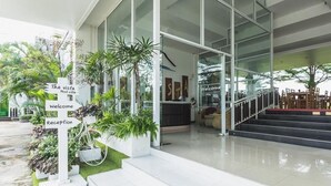 Entrada de hotel moderna com balcão de recepção, portas de vidro e escada que leva ao andar superior.