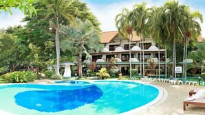 Hotel com piscina rodeada por vegetação exuberante e palmeiras.