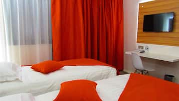 Quarto de hotel com duas camas, uma escrivaninha, uma cadeira e uma televisão na parede.