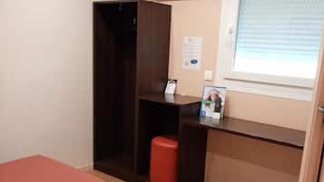 Quarto de hotel com duas camas, televisão presa na parede, janela com persianas e uma pequena mesa de trabalho com cadeira.