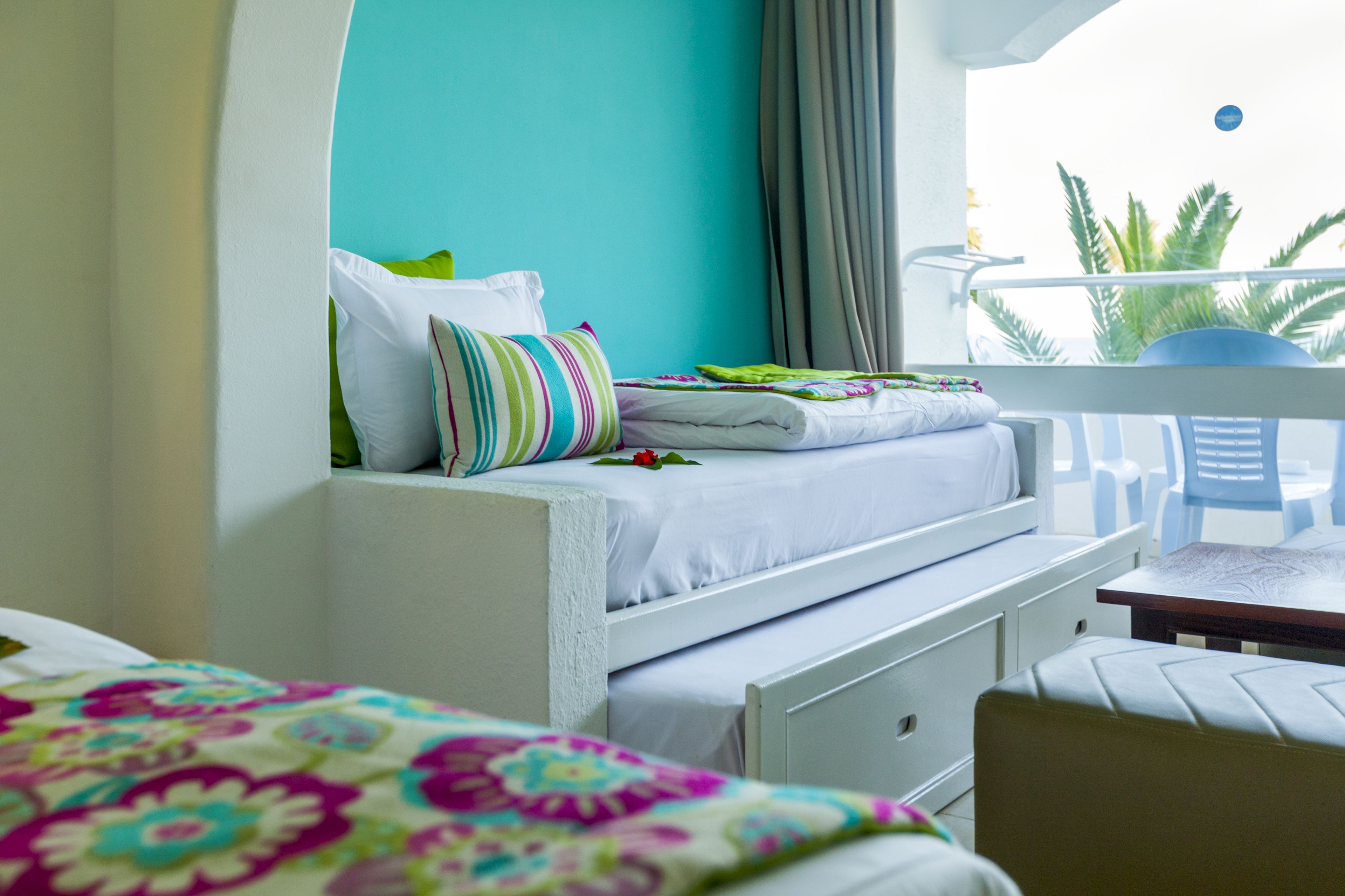 Quarto com cama, uma mesinha e vista para palmeiras.