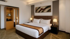 Quarto de hotel com uma cama grande, duas mesas de cabeceira com abajures, um guarda-roupa e um quadro na parede.