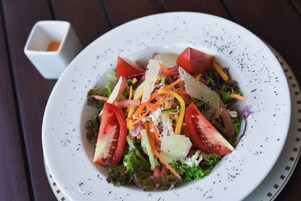 Uma salada com diversos vegetais e um pequeno recipiente com molho.