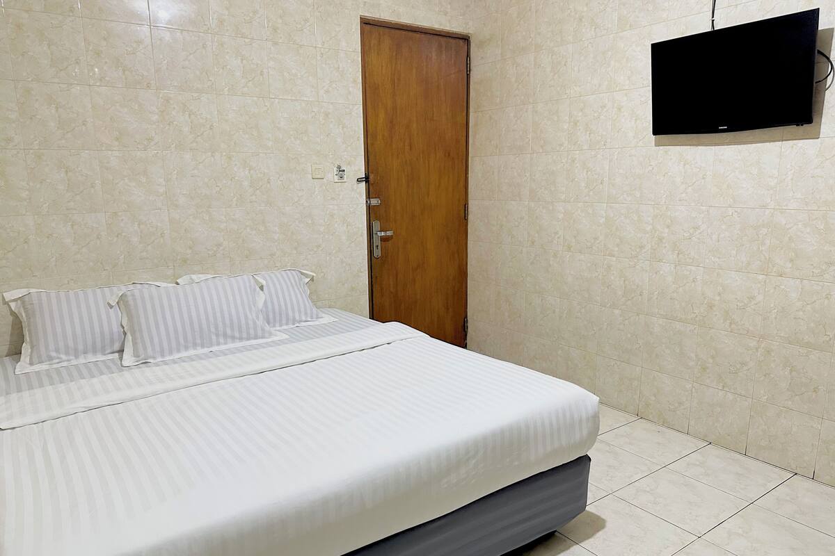 Um quarto com cama, porta de madeira e televisão de tela plana na parede.