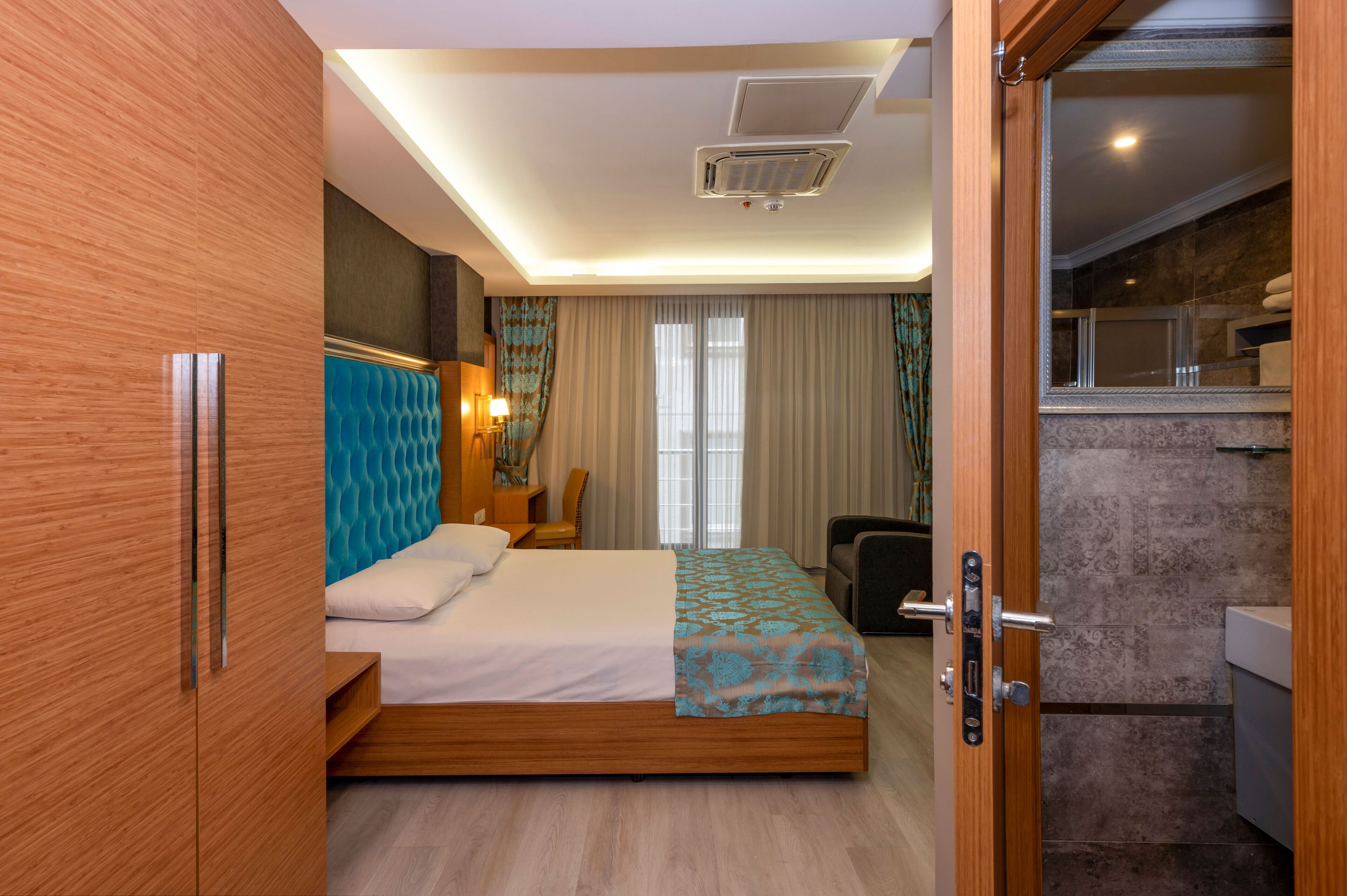 Quarto de hotel moderno com cama de madeira, uma escrivaninha e um banheiro visível através de uma porta aberta.