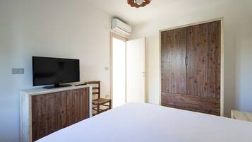 Quarto com cama, televisão sobre um armário de madeira, uma cadeira e um guarda-roupa.