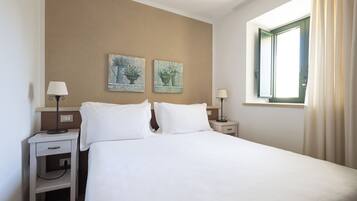 Quarto de hotel com uma cama, duas mesas de cabeceira, duas luminárias e duas pinturas penduradas na parede.