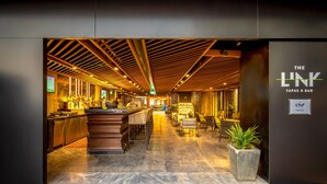 Uma área de bar moderna com teto de madeira, balcão, assentos e um letreiro com a inscrição 'THE LINK TAPAS & BAR'.