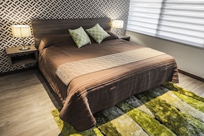 Quarto bem arrumado com cabeceira estampada, duas luminárias de apoio e um tapete com padrão geométrico.