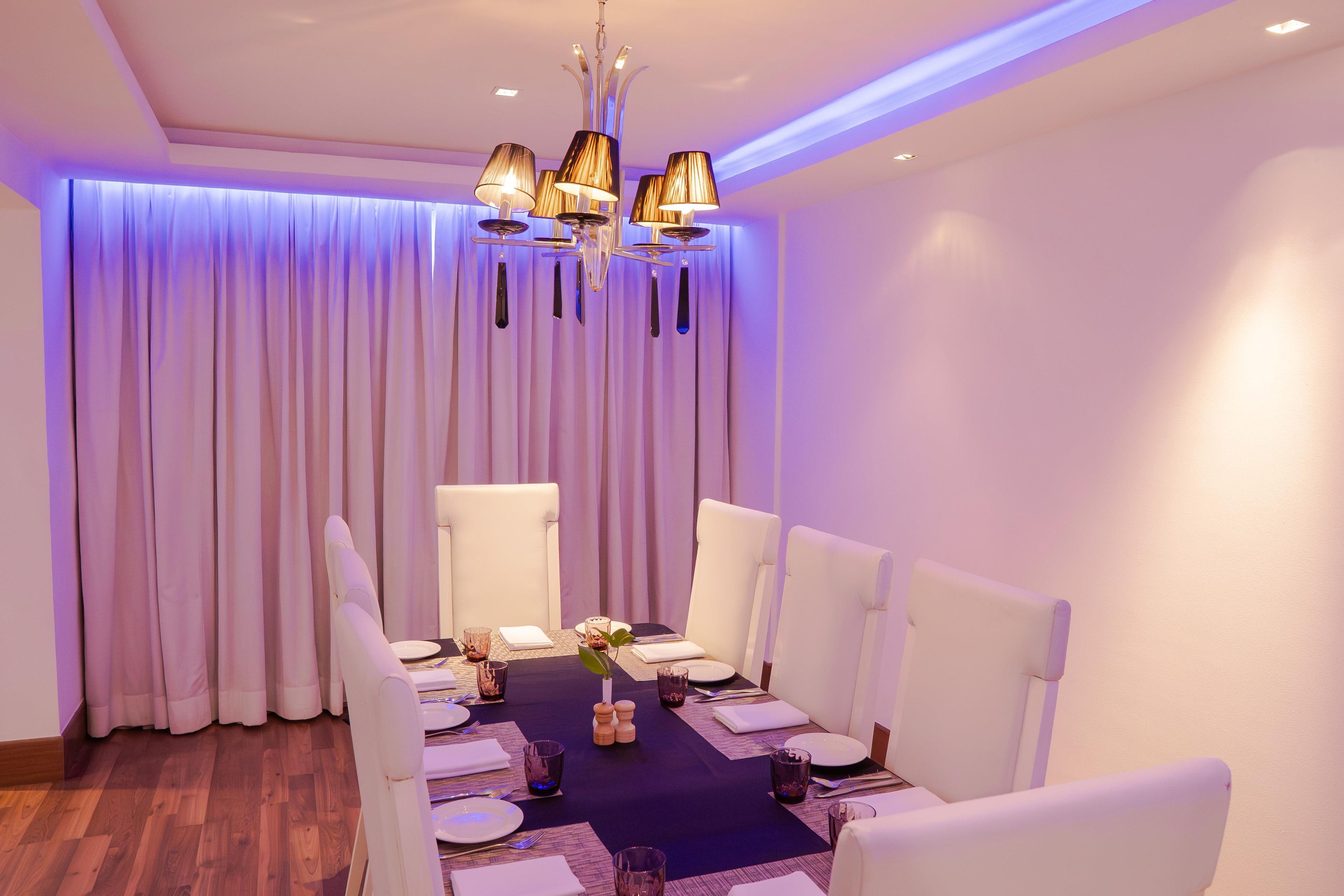 Uma sala de jantar com uma mesa comprida posta para refeição, rodeada por cadeiras brancas, com um lustre acima.