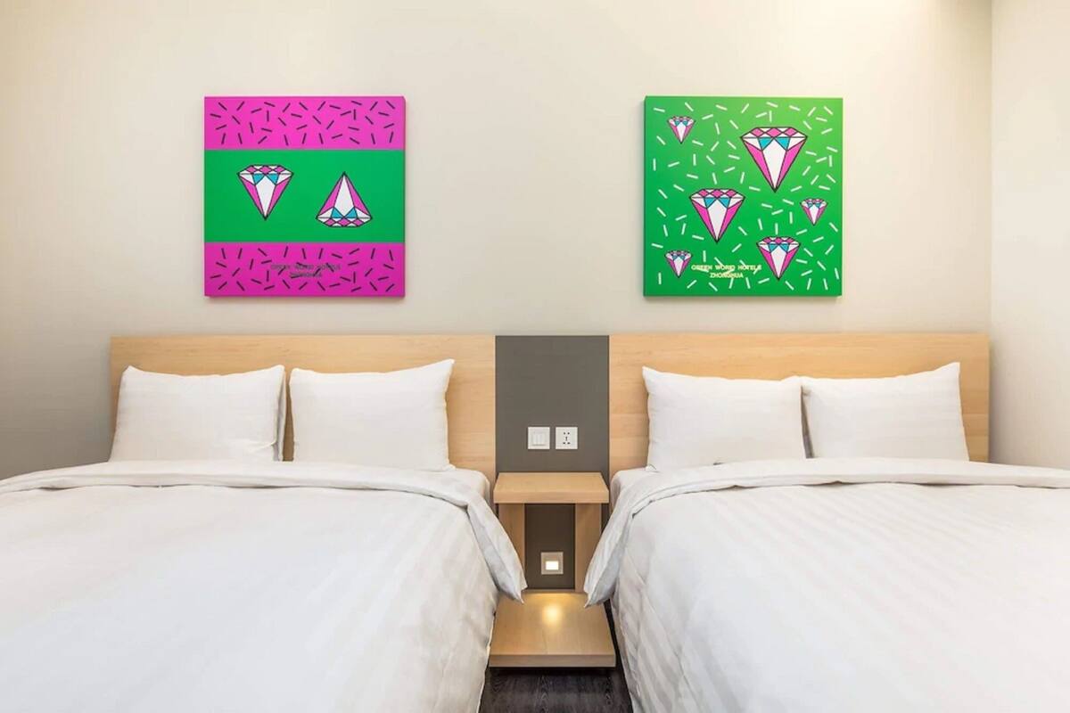 Quarto de hotel com duas camas, uma mesa de cabeceira e duas obras de arte na parede retratando diamantes.