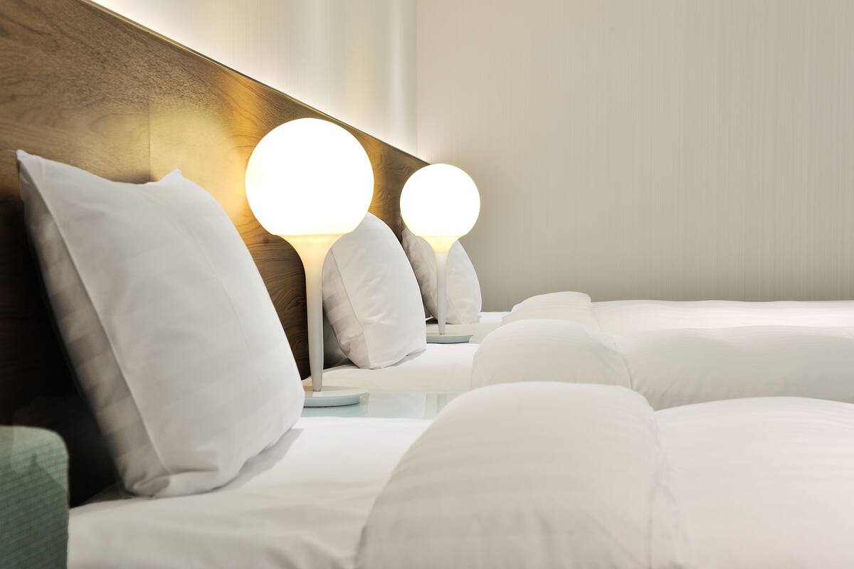 Quarto de hotel com cama bem arrumada, duas luminárias de cabeceira e cabeceira de madeira.