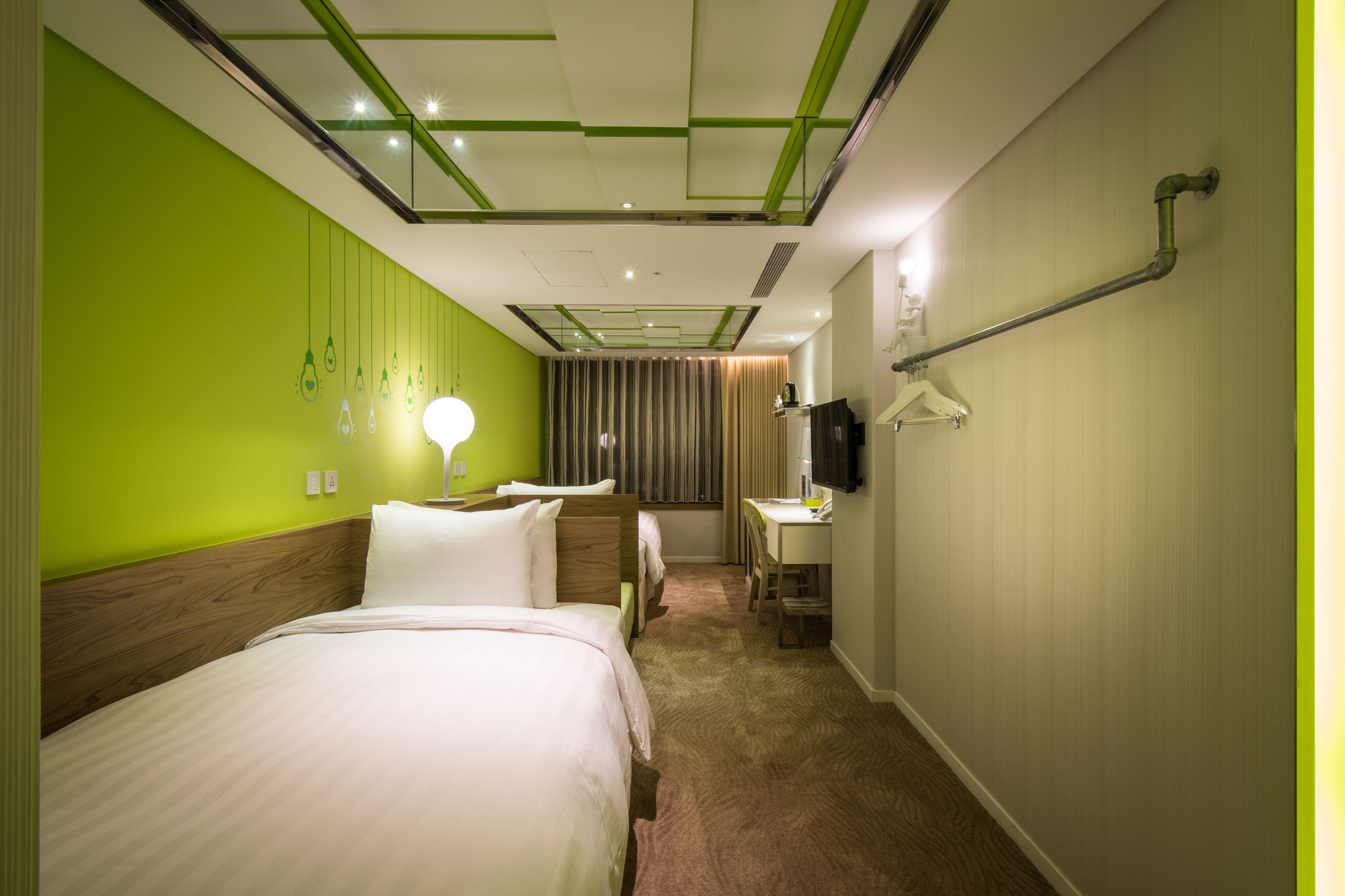 Quarto de hotel com duas camas, uma escrivaninha, um espelho e uma televisão.